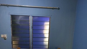 Quarto com cama de madeira, janela com grades de metal, mesa de cabeceira e piso estampado.