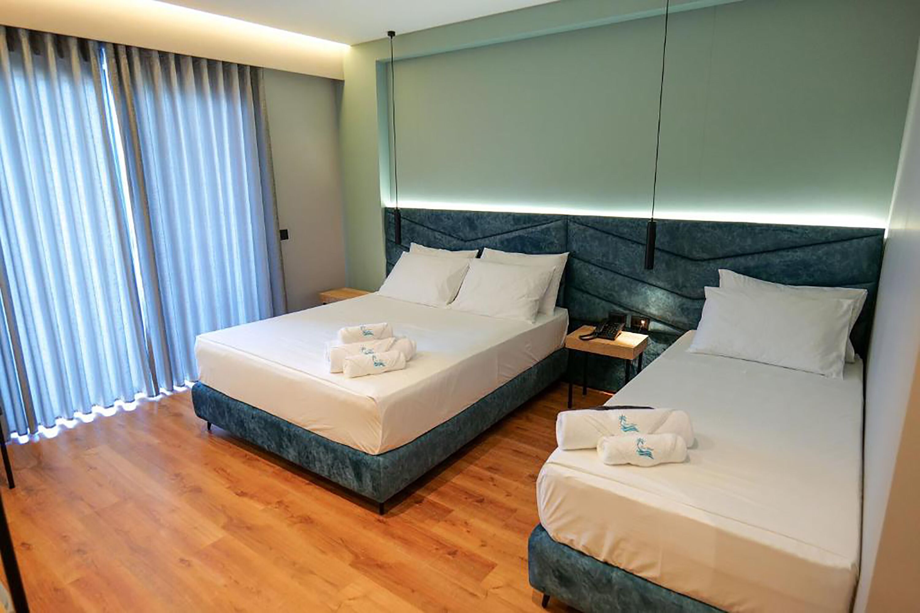 Quarto de hotel com duas camas, piso de madeira e uma grande janela com cortinas.