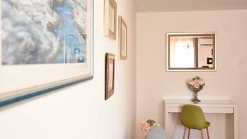 Quarto com escrivaninha branca, cadeira verde, quadro emoldurado e um vaso com flores.