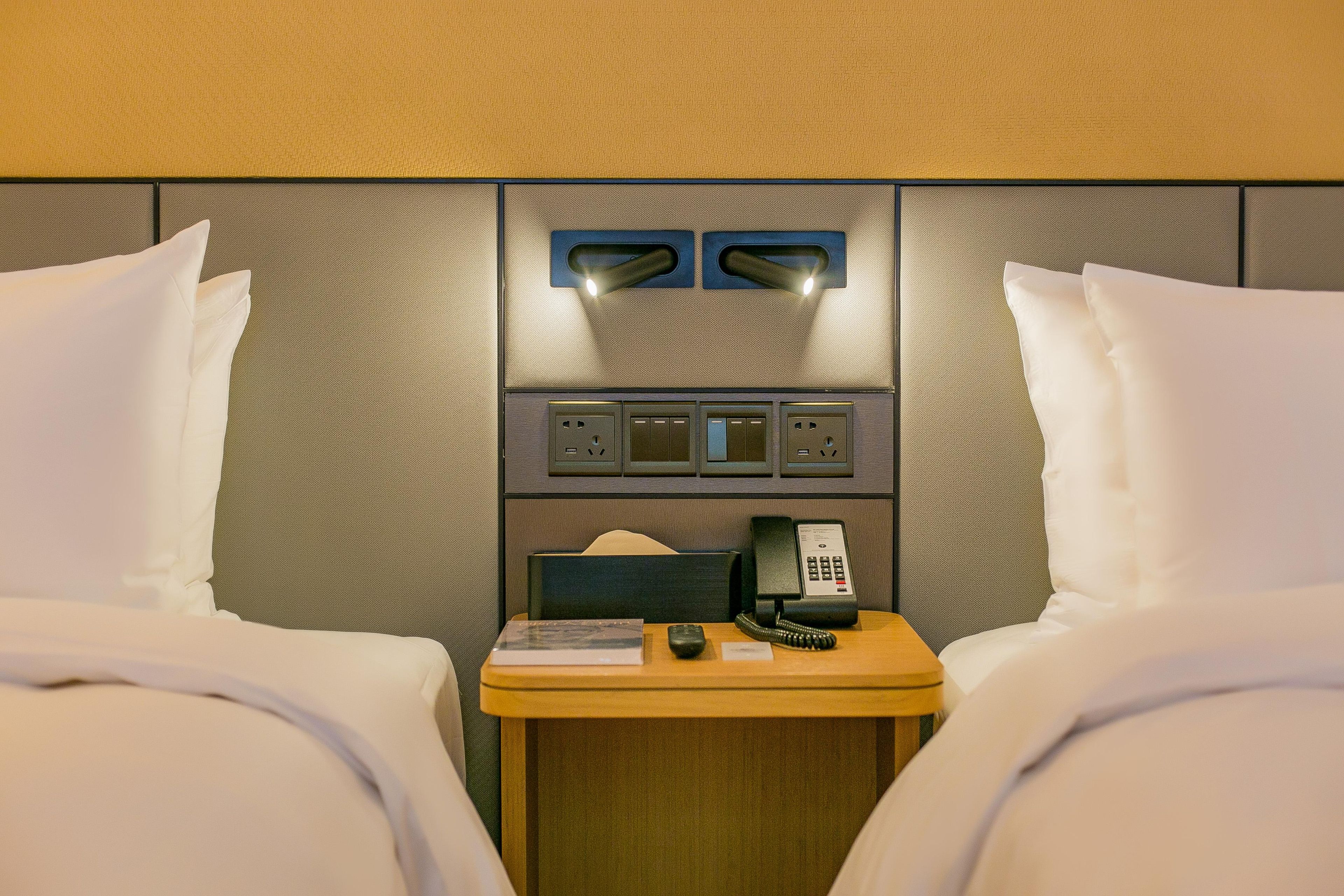 Quarto de hotel com duas camas, uma mesa de cabeceira com telefone, abajur e uma pequena caixa.