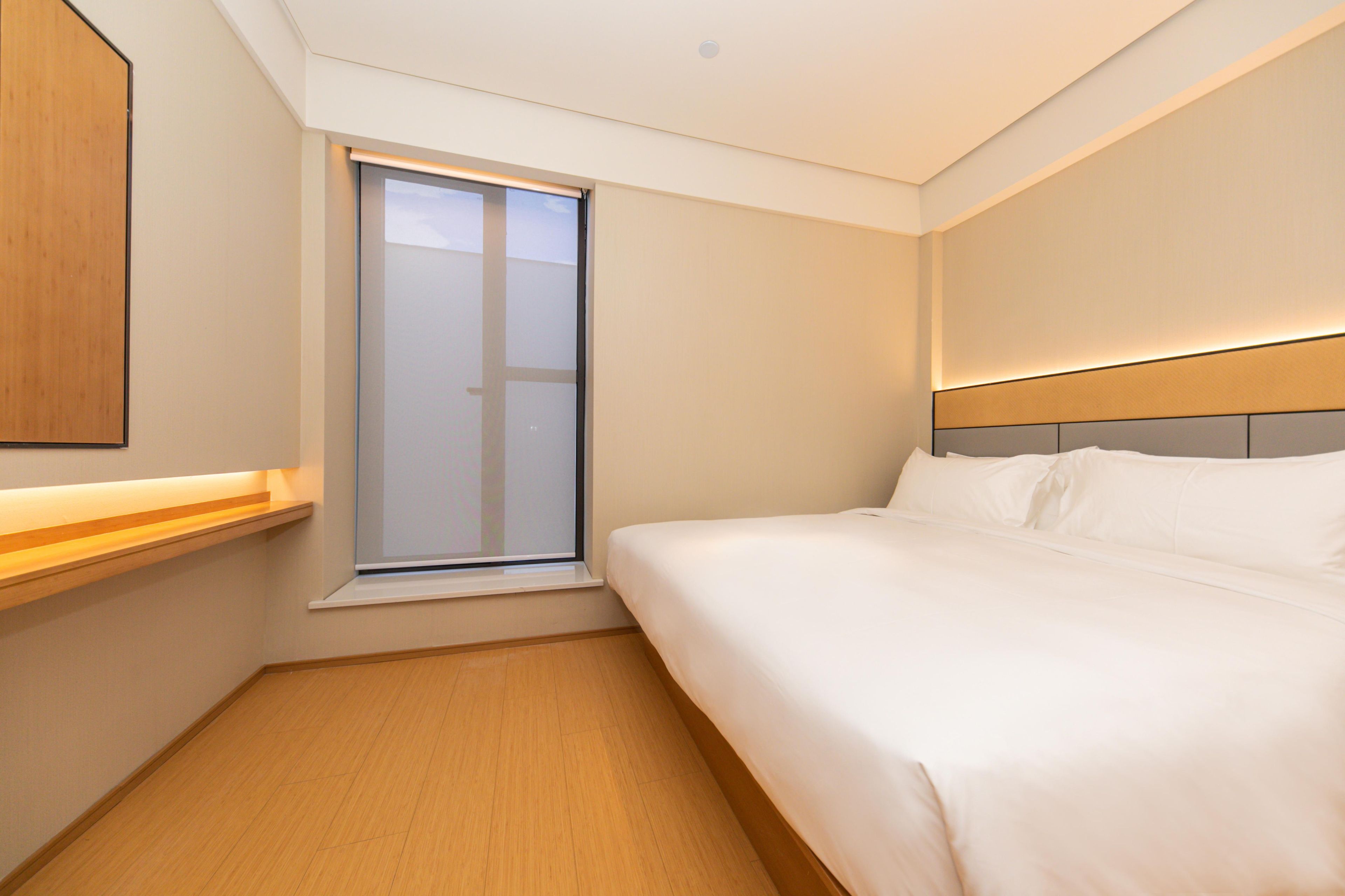 Quarto de hotel com cama, janela e piso de madeira.