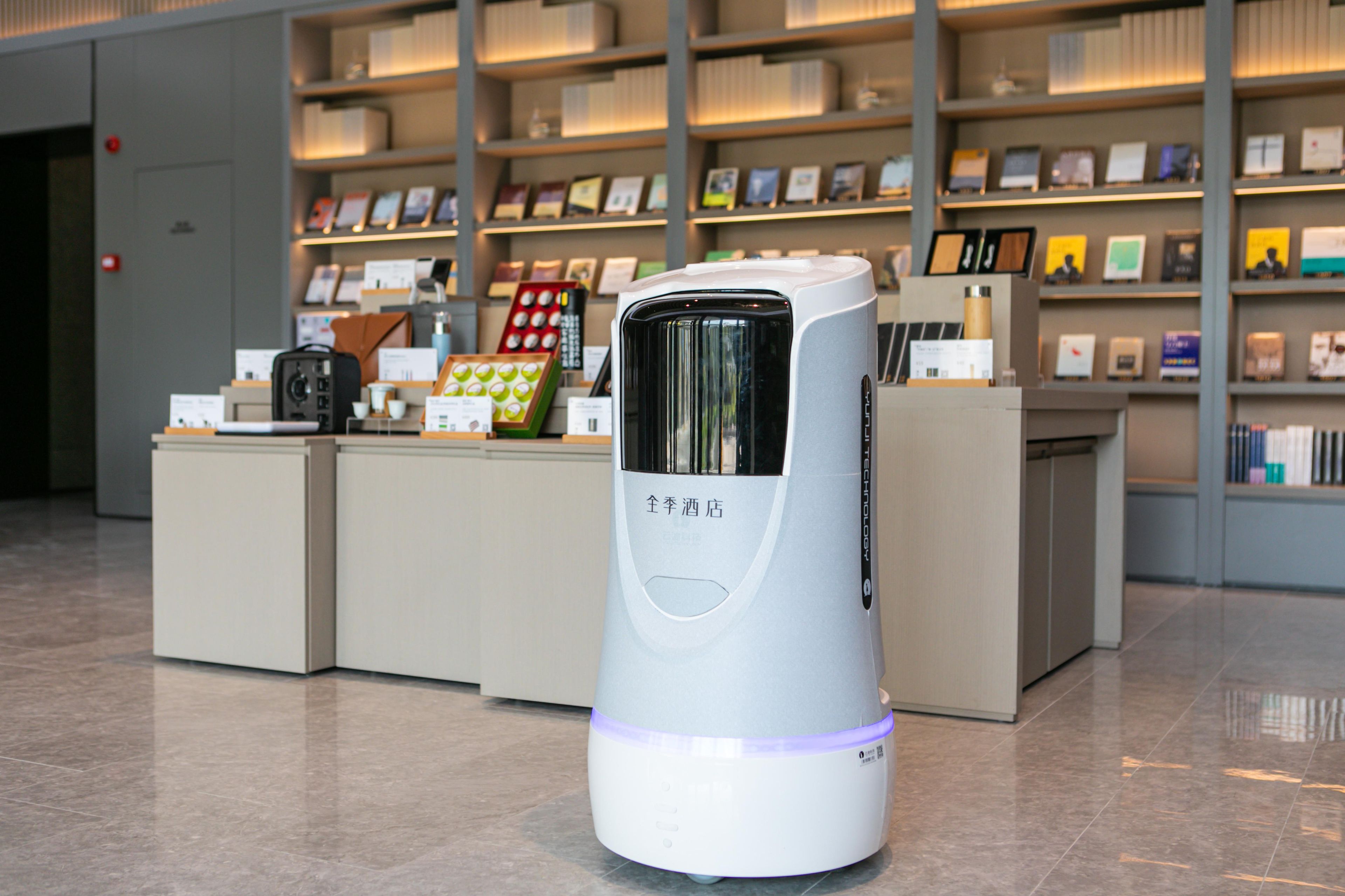 Uma área de recepção de hotel moderna, com um objeto cilíndrico branco grande em primeiro plano, provavelmente um equipamento ou item decorativo.