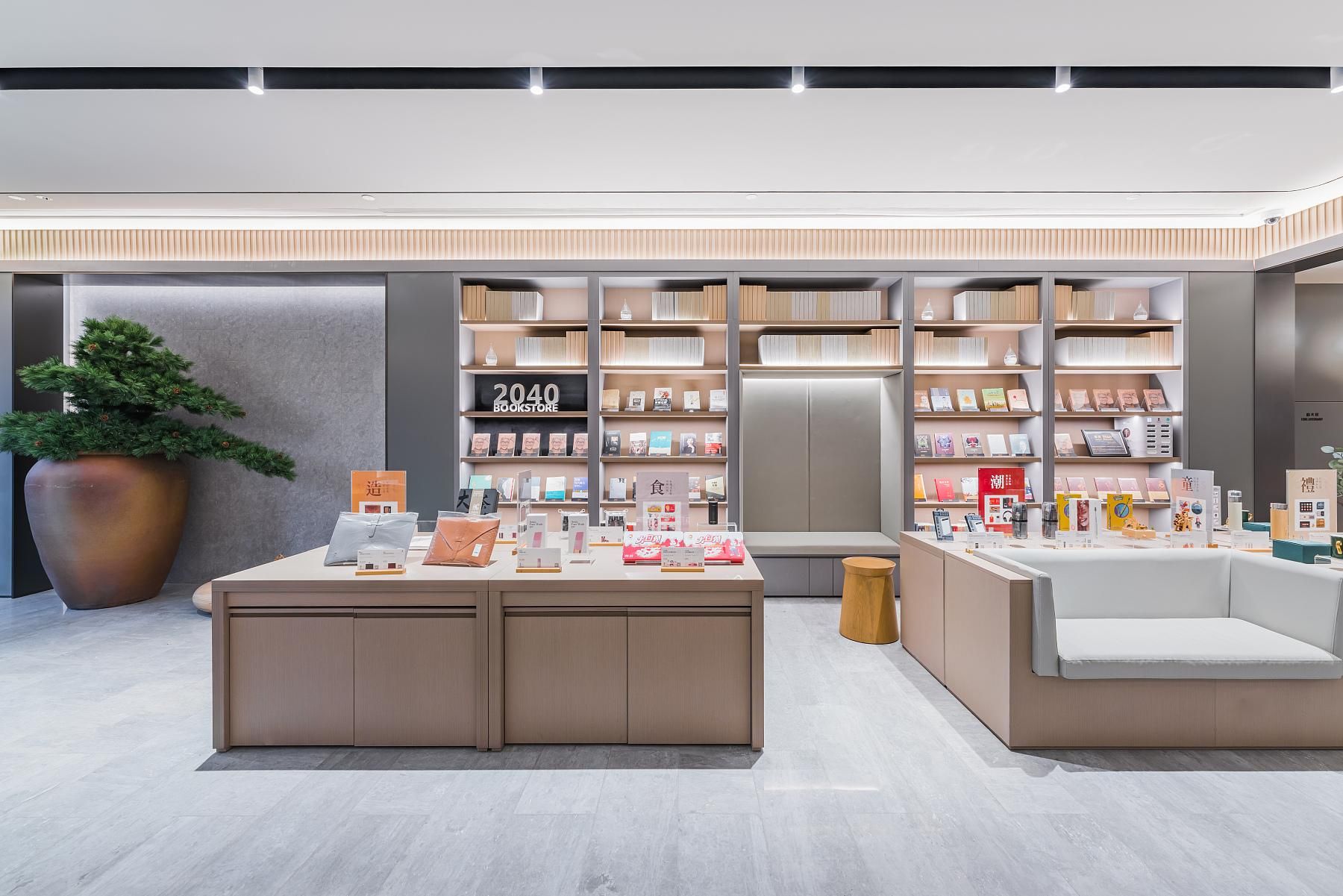 Uma livraria moderna com uma mesa de exposição central, estantes com livros e uma grande planta em vaso.