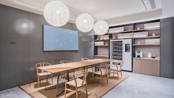 Uma sala de reunião moderna com uma mesa comprida, cadeiras, uma tela grande e um refrigerador.