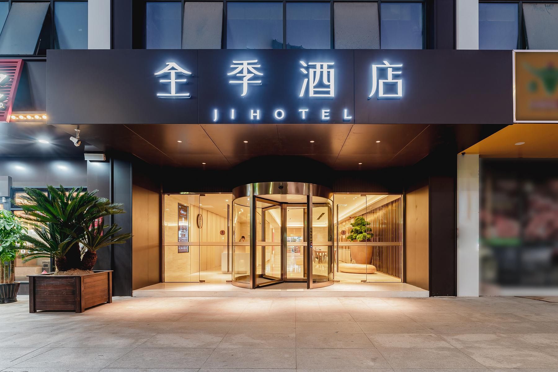 Entrada de hotel com design moderno, destacando uma porta de vidro e uma placa com letras iluminadas.