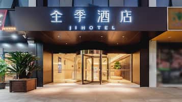 Entrada de hotel com design moderno, destacando uma porta de vidro e uma placa com letras iluminadas.