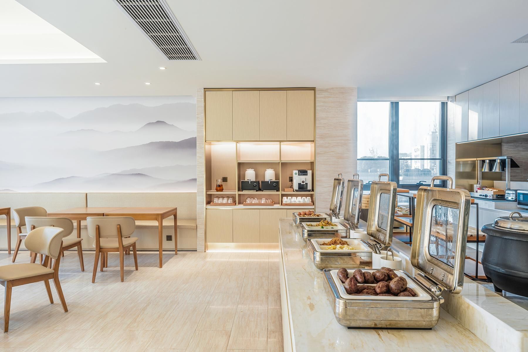 Uma área de refeições moderna em hotel, com buffet, mesas e vista para a cidade.