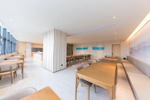 Uma sala de conferências moderna com uma mesa comprida, várias cadeiras, uma copa e uma área de estar com vista.
