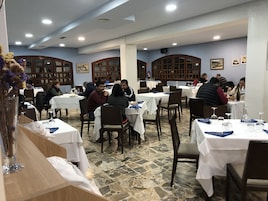 Restaurante com várias mesas, cadeiras e chão de azulejos.