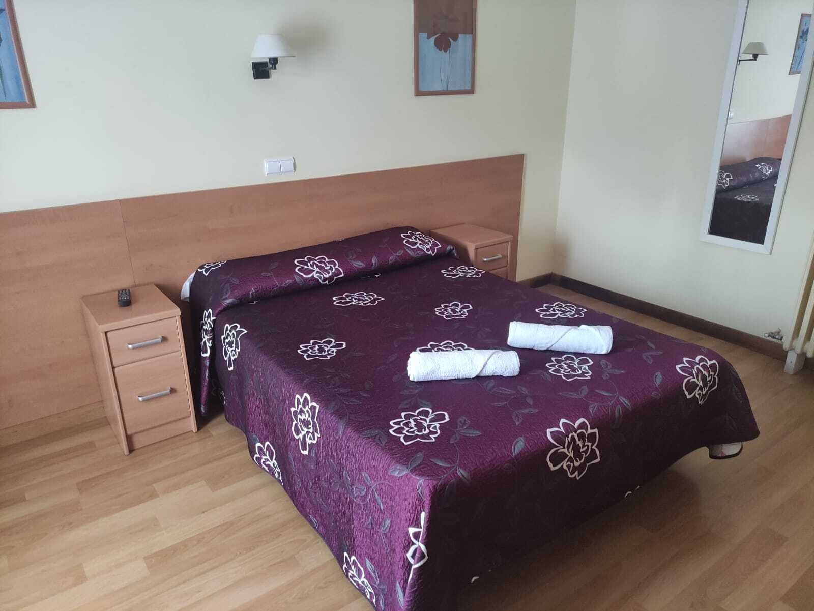 Quarto de hotel com uma cama, duas mesas de cabeceira, um criado-mudo, uma luminária na parede e um quadro emoldurado.