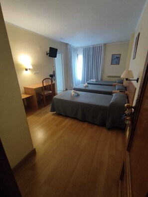 Quarto de hotel com duas camas, uma mesa, uma cadeira, uma televisão e uma janela com cortinas.