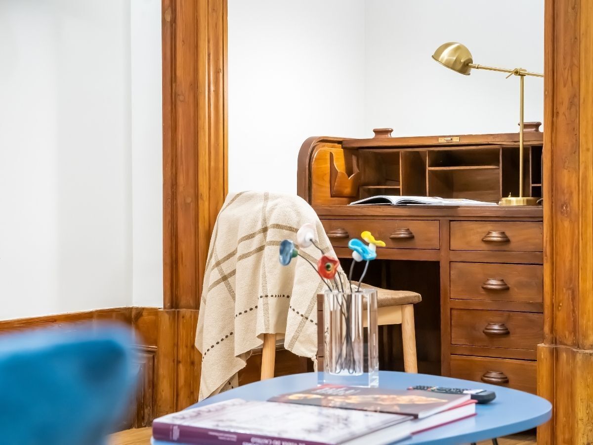 Uma sala de estudos com uma mesa de madeira, uma cadeira, uma luminária e uma estante.