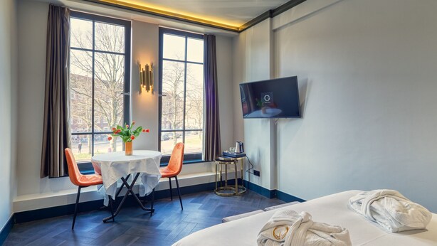 Quarto de hotel com cama, televisão na parede, mesa com cadeiras e janela com cortinas.