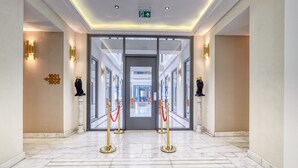 Um saguão de hotel com piso de mármore, estacas douradas e entrada de vidro.