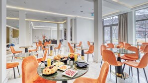 Uma sala de jantar moderna com mesas redondas e cadeiras laranja, com opções de pequeno-almoço e chão em mármore.