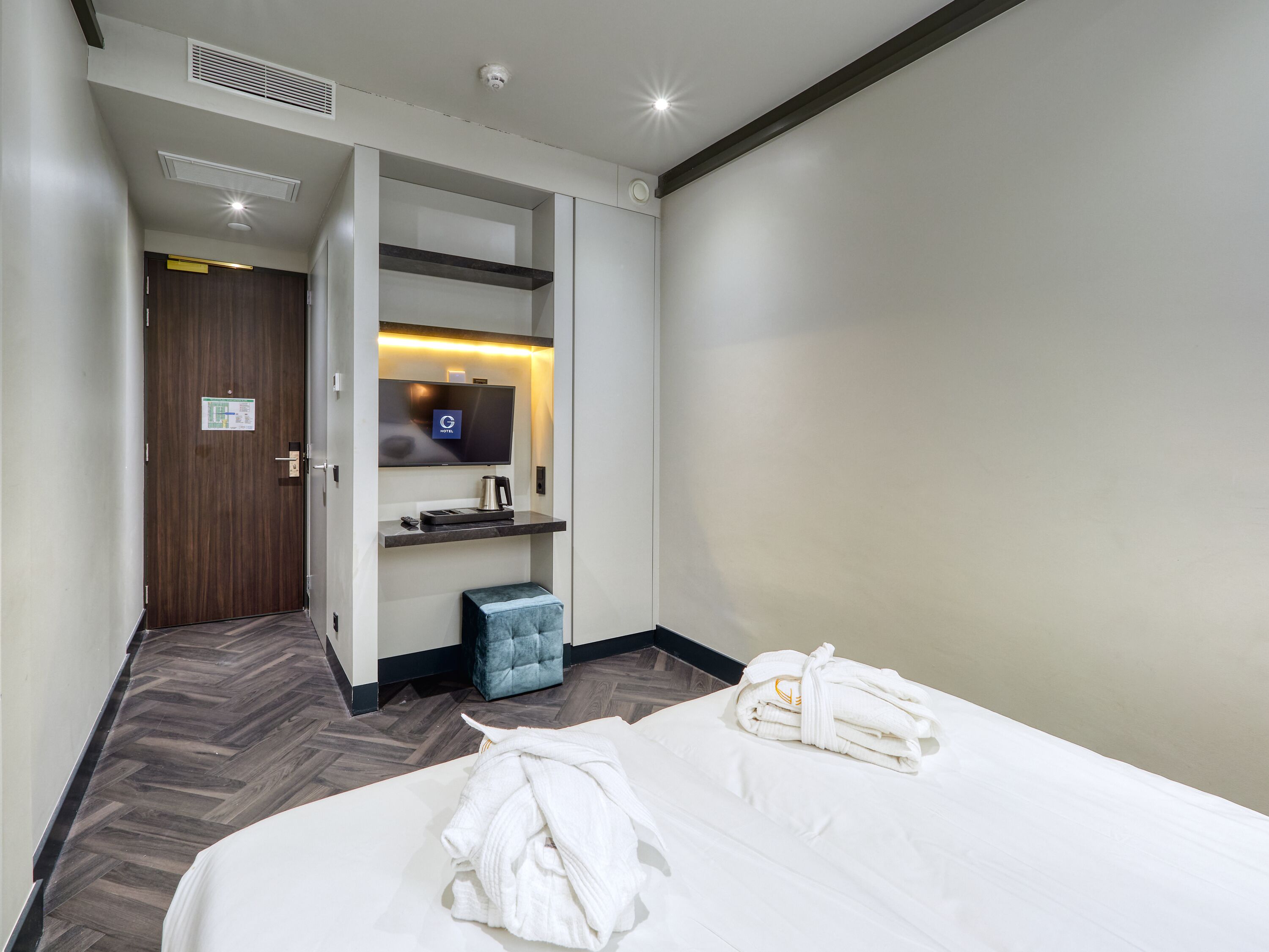 Quarto de hotel com cama, televisão, minibar e um pequeno espaço para sentar.