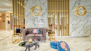 Um hall luxuoso com piso de mármore, um sofá de couro macio, uma mesa de centro de vidro com uma escultura de gato e almofadas decorativas.