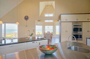 Cozinha moderna com uma ilha grande, eletrodomésticos de aço inoxidável e vista para a praia.