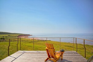 Um deck de madeira com uma cadeira e binóculos, com vista para uma praia e um penhasco.