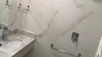 Um banheiro moderno com piso e paredes de mármore, pia, espelho e chuveiro com chuveiro manual.
