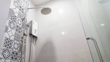 Área de chuveiro com chuveiro manual, painel de controle fixado na parede e box envidraçado.