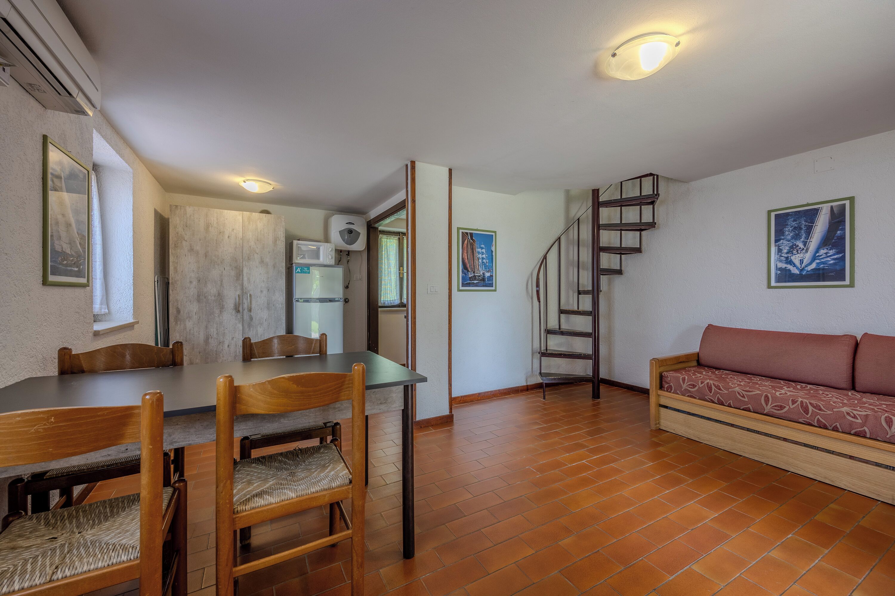 Uma área de refeições com uma mesa e cadeiras de madeira, uma cozinha com micro-ondas e uma escada que dá para outro andar.