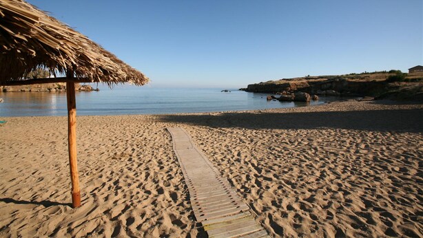 Uma praia arenosa com uma estrutura de telhado de palha e um caminho de madeira que leva à água.