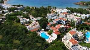 Vista aérea de uma área de resort à beira-mar, com vários edifícios, uma grande piscina e vista para o mar.