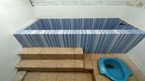 Um banheiro com banheira azul listrada, degraus bege estampados e vaso sanitário azul.