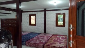 Quarto com parede de tijolos brancos, duas janelas e uma porta de madeira. Três colchões com estampas florais no chão.