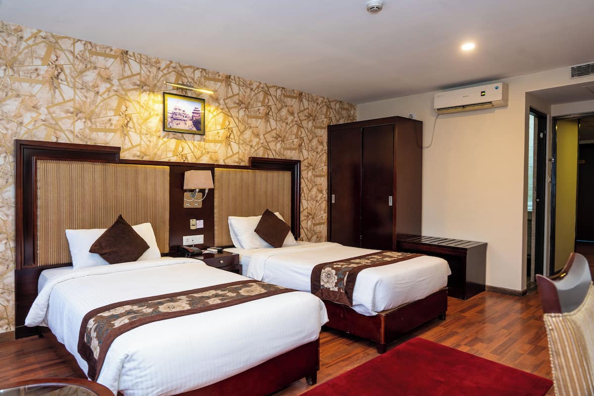 Quarto de hotel com duas camas, uma escrivaninha, um guarda-roupa e um ar condicionado.