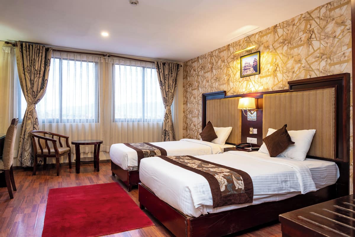 Quarto de hotel com duas camas, um tapete vermelho, móveis de madeira e parede estampada.