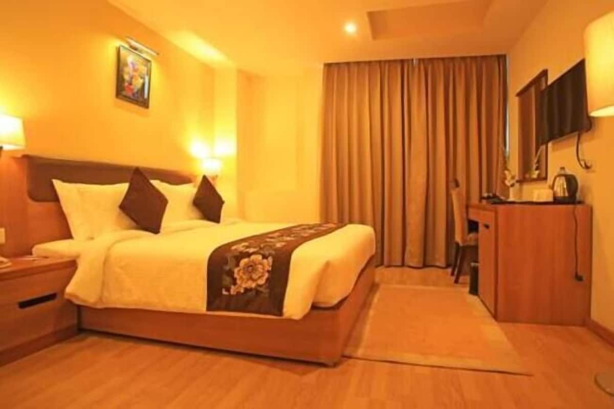 Quarto de hotel com cama, mesa de cabeceira, abajur e escrivaninha com cadeira.