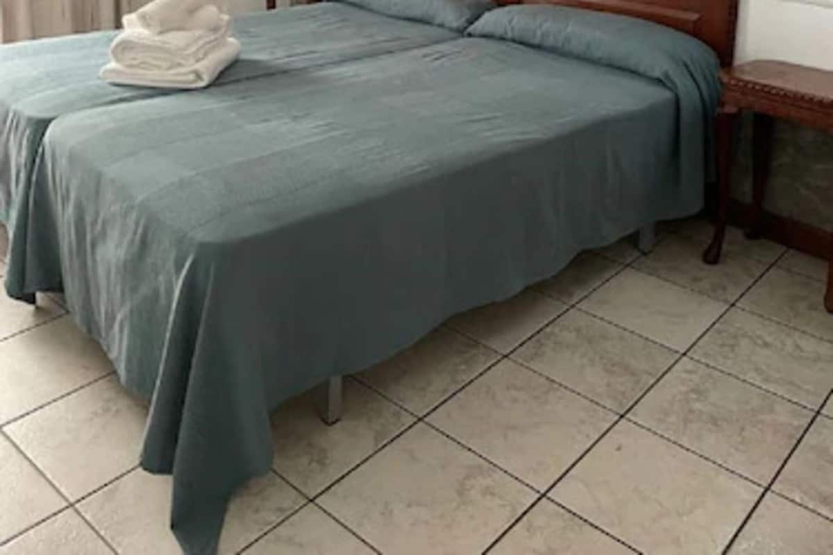 Quarto de hotel com uma cama de casal, uma mesinha de cabeceira, uma luminária e um quadro na parede.