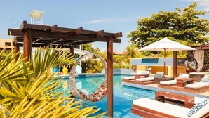 Área de piscina com espreguiçadeiras, pérgola e rede.