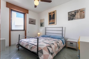 Um quarto com cama, mesa de cabeceira, janela e quadros nas paredes.