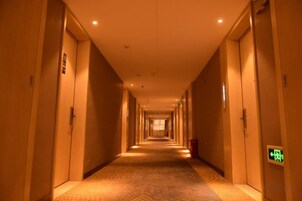 Corredor de hotel com portas em ambos os lados, carpete estampado e placas de saída de emergência.