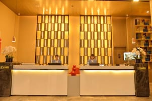 Balcão de recepção com dois recepcionistas, um balcão de check-in e uma parede com padrão geométrico.