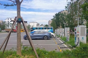 Área de estacionamento com estações de carregamento para veículos elétricos, um ônibus e uma árvore.