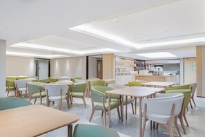 Uma área de jantar moderna com várias mesas e cadeiras, uma cozinha ao fundo e um design limpo e contemporâneo.