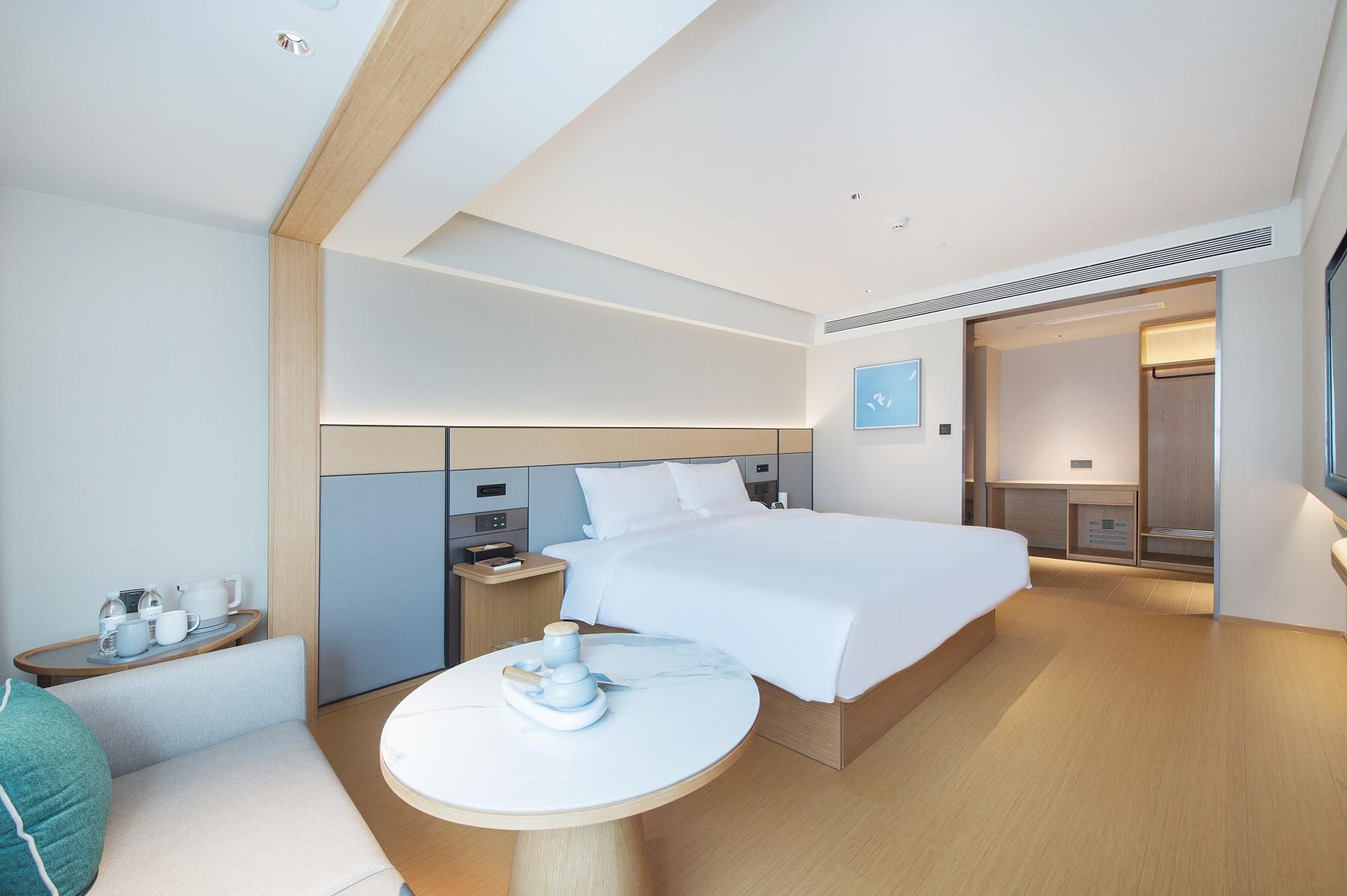 Quarto de hotel moderno com uma cama grande, mesas de cabeceira, uma mesa de centro redonda e um closet espaçoso.