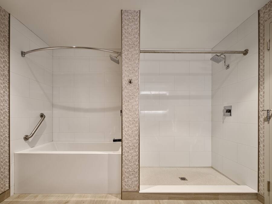 Uma casa de banho com banheira e cabine de duche, ambos com azulejos brancos e uma moldura estampada.