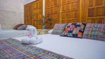 Quarto de hotel com duas camas, um guarda-roupa de madeira e uma mesinha de cabeceira com um vaso de flores.