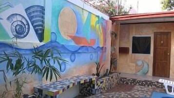 Um edifício com um mural colorido na parede externa, uma porta e uma pequena área externa com uma mesa e cadeiras.