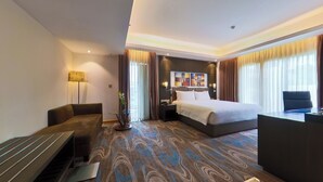 Quarto de hotel com cama, escrivaninha, cadeira, luminária e janela com cortinas.