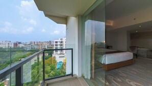 Quarto moderno com cama grande, varanda com grade de vidro e vista para a cidade.