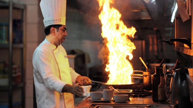 Um cozinheiro de uniforme branco cozinha usando chamas.