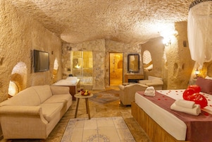 Quarto com parede de pedra, banheira, sofá, mesa com frutas e cama com balões vermelhos.