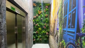 Um corredor estreito com parede texturizada, jardim vertical verde e um mural de bicicleta.