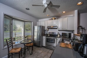 Uma cozinha moderna com armários brancos, eletrodomésticos de aço inoxidável, um espaço de refeições com cadeiras de vime e um ventilador de teto.